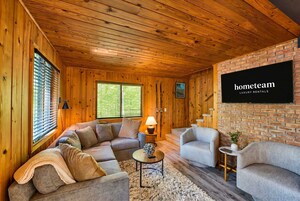 Um quarto acolhedor com paredes e teto de madeira, um sofá, uma mesinha e uma TV fixada numa parede de tijolos.