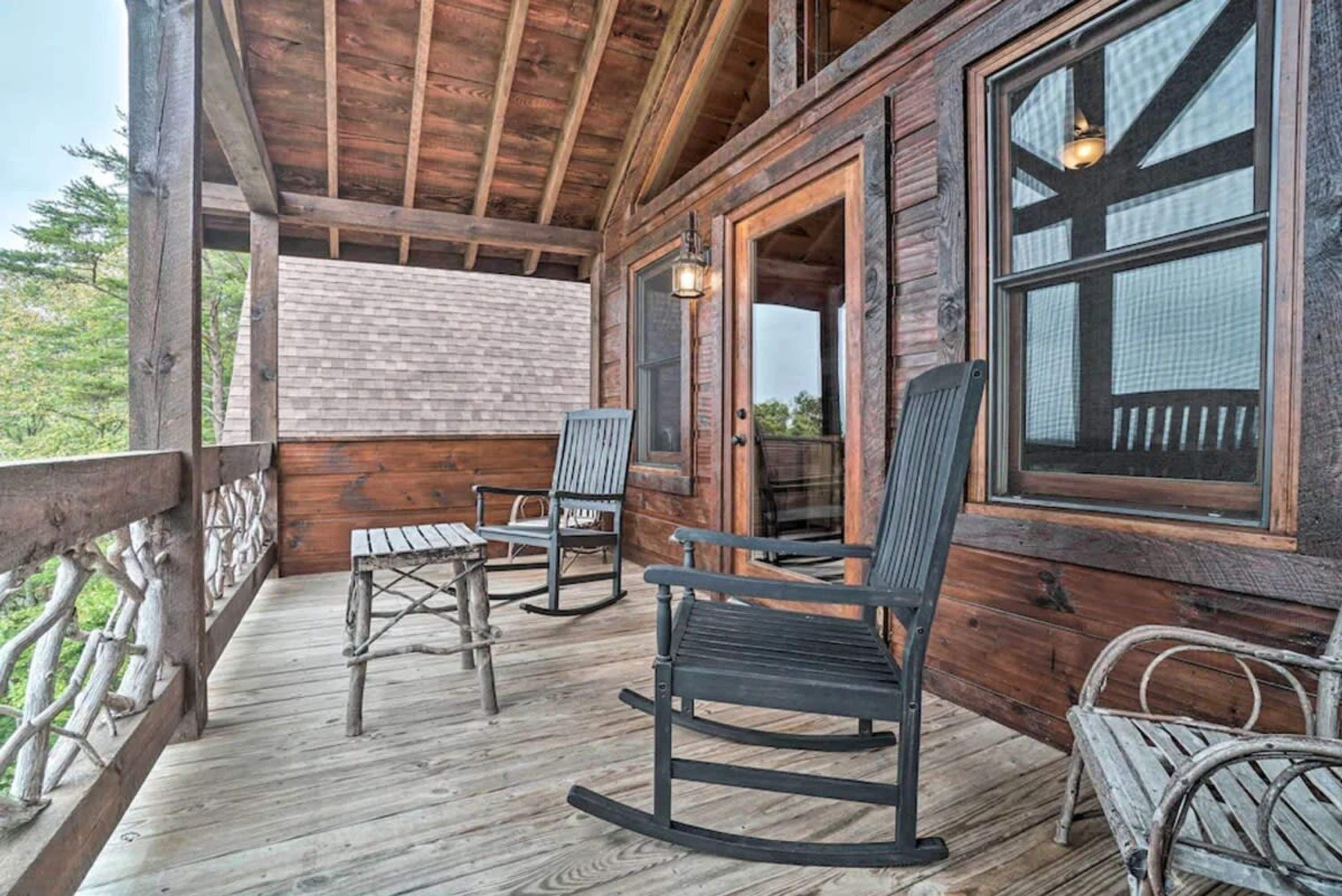 Varanda de madeira com duas cadeiras de balanço e uma mesa, um muro de tijolos e uma janela com vista para o exterior.