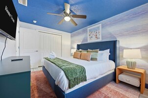 Quarto com cama, mesa de cabeceira, escrivaninha, ventoinha no teto, porta e parede com textura.
