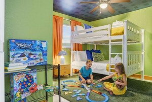 Um quarto infantil com beliches, uma escrivaninha cheia de brinquedos e um ventilador de teto.