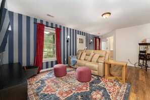 Quarto com paredes listradas, um sofá, pufes, uma mesa e um abajur.
