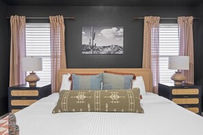 Quarto com uma cama, duas mesas de cabeceira, um quadro na parede e cortinas.