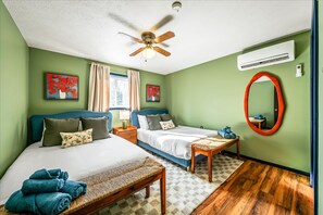 Quarto de hotel com duas camas, ventoinha no teto, ar condicionado, espelho e obras de arte nas paredes.