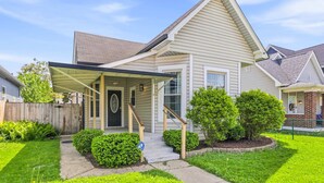 A two-story house with a covered front porch, a front yard with a lawn and shrubs, and a neighboring house with a similar architectural style.