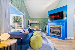 Uma sala de estar com lareira azul, televisão montada acima e uma janela com cortinas.