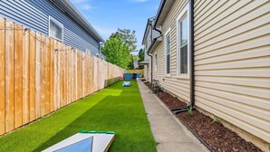 A residential backyard with a wooden fence, artificial grass, and a concrete pathway.