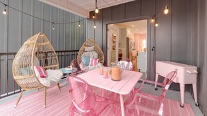 Um pátio externo com cadeiras de vime, uma mesa rosa e um ventilador de teto.