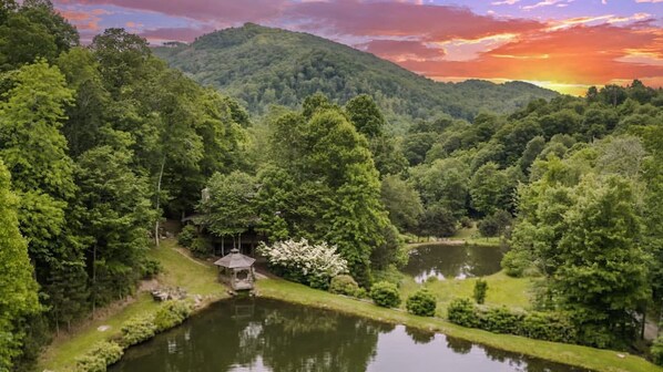 Uma paisagem tranquila com lago, vegetação exuberante e um pequeno coreto.