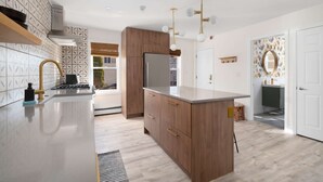 Uma cozinha moderna com ilha central, armários de madeira, geladeira de aço inoxidável e backsplash estampado.