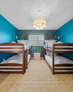 Quarto com beliches, parede estampada, luminária no teto e janela com persianas.