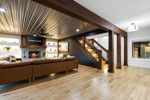 Uma sala de estar moderna com lareira de pedra, um amplo sofá de canto e uma escadaria com vigas de madeira.