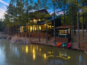 Uma cabana à beira do lago com varanda, área externa coberta e um píer com caiaques.