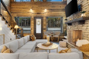 Interior de uma cabana de tronco com sala de estar, sofá, lareira e escada.