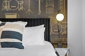 Quarto com cama, travesseiros, cabeceira e parede com ilustrações de instrumentos musicais.