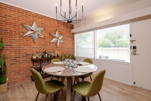 Uma sala de jantar com parede de tijolos, decorações em formato de estrela, um candelabro e uma janela com persianas.