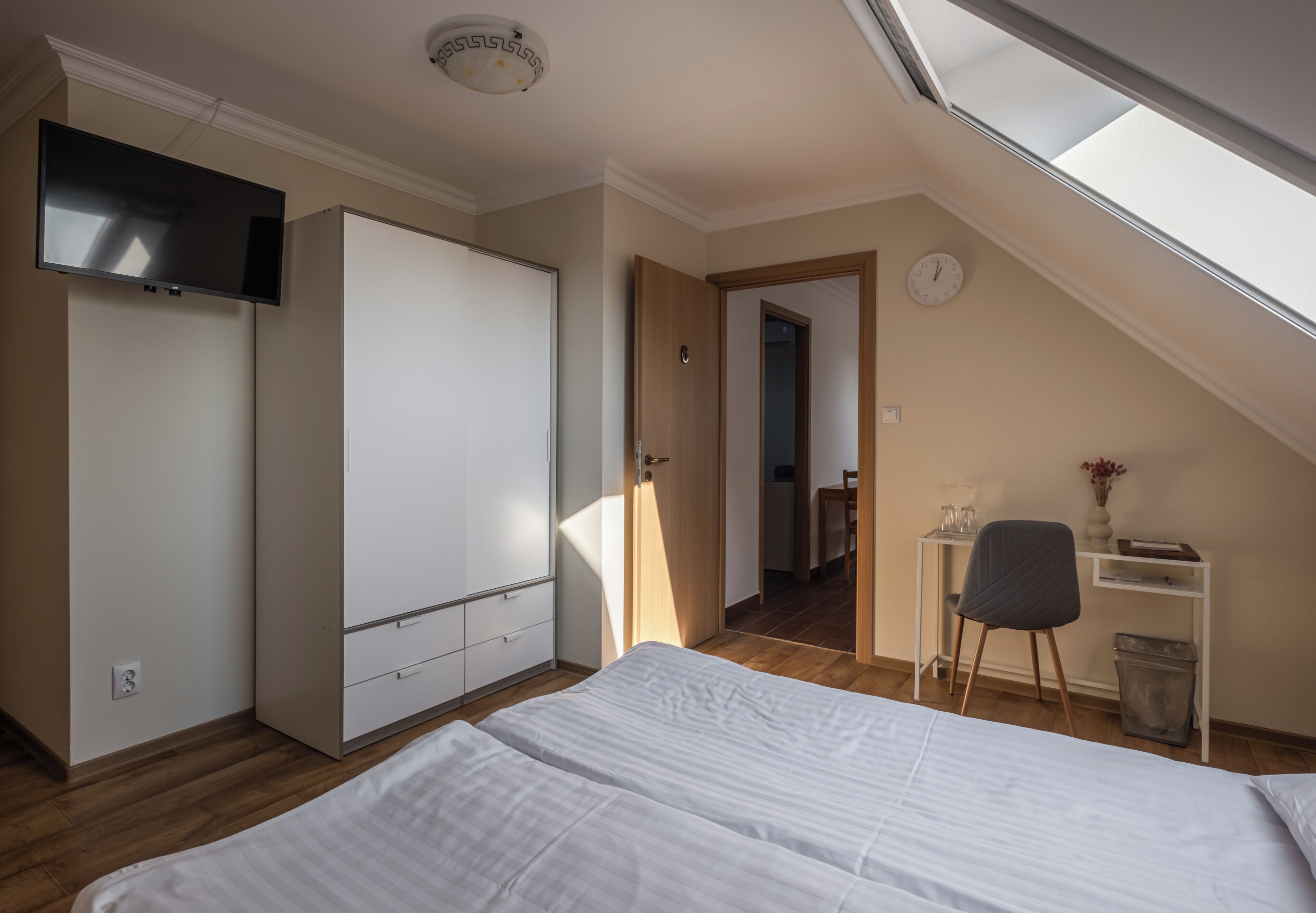 Quarto com cama, guarda-roupa, escrivaninha, cadeira e clarabóia.