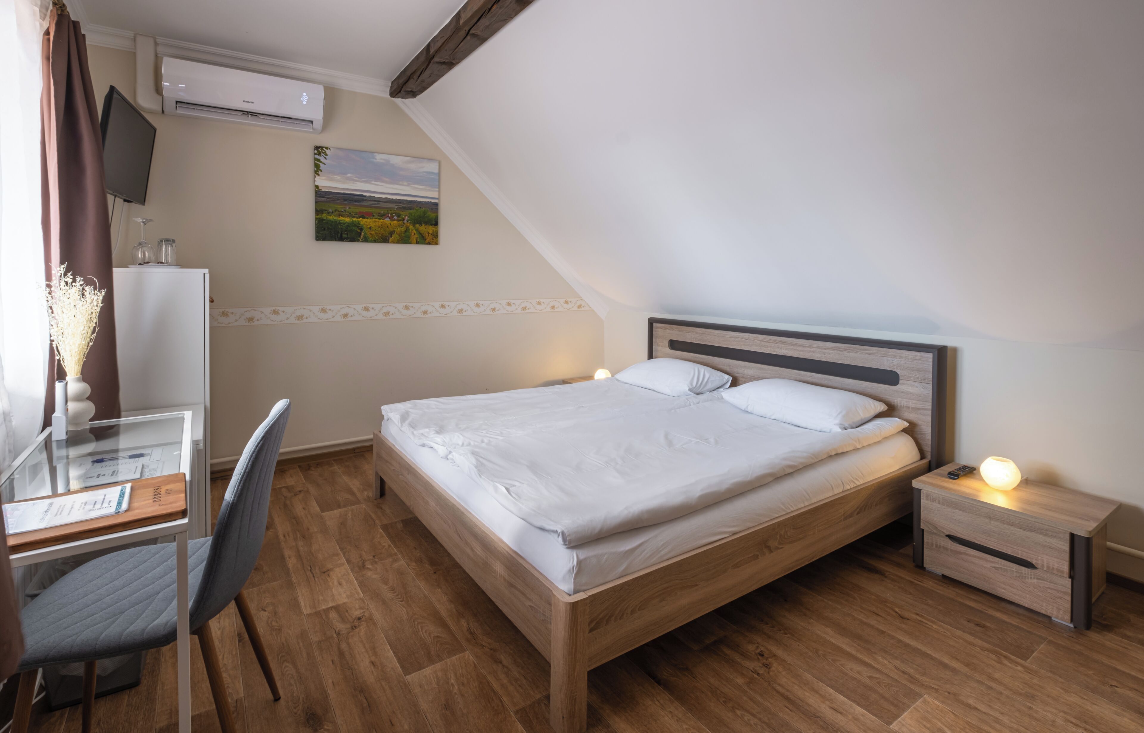 Um quarto com uma cama de madeira, uma escrivaninha com cadeira, ar condicionado e um quadro na parede.
