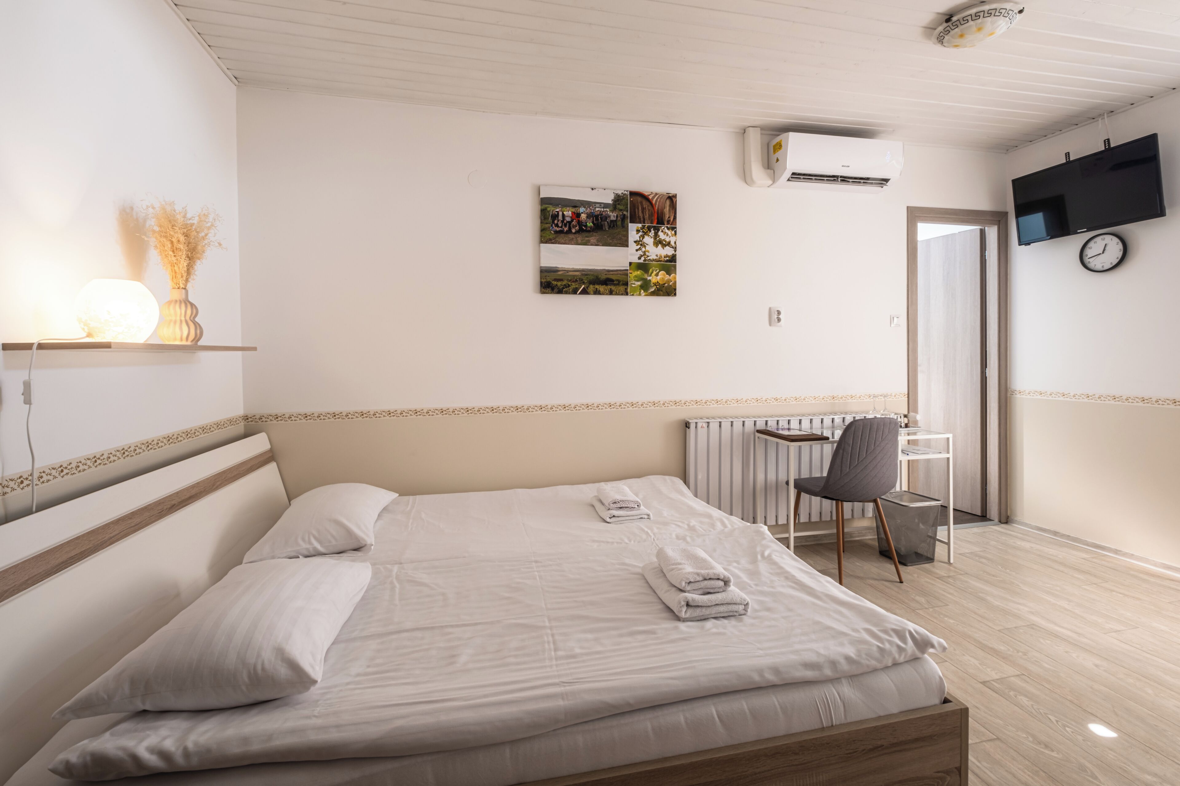 Quarto com cama, escrivaninha, cadeira, televisão na parede e radiador.
