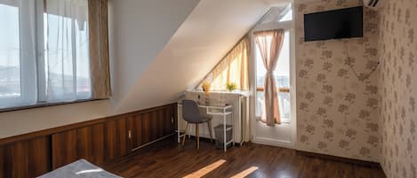 Quarto com teto inclinado, uma cama, uma escrivaninha e uma TV fixada na parede.