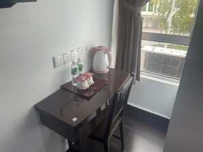 Uma pequena mesa com uma chaleira, um sabonete líquido e um porta-guardanapos vermelho em um quarto com janela e vista para uma varanda.