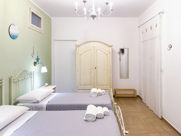 Quarto de hotel com duas camas, um candelabro, um guarda-roupa e um espelho.