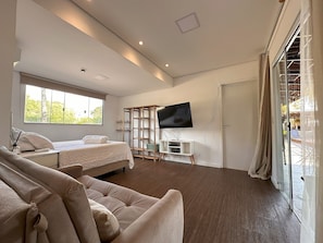 Quarto de hotel moderno com uma cama grande, um sofá, uma TV na parede e uma janela com vista para o verde.