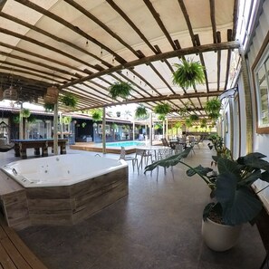 Área externa coberta com hidromassagem, assentos e plantas em vasos.