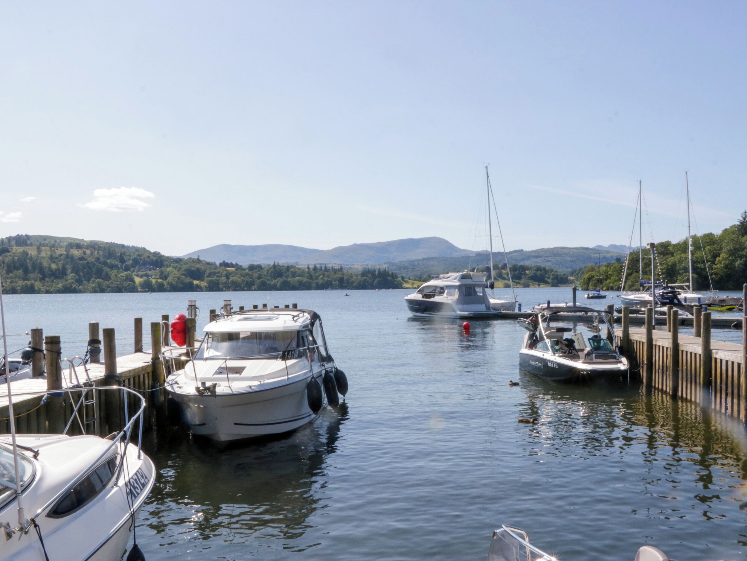 Uma marina com barcos atracados, água calma e uma paisagem montanhosa ao fundo.