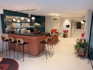 Uma área de bar moderna com balcão curvo, banquetas e uma variedade de garrafas e copos.