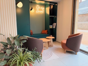 Um espaço de estar aconchegante, com uma luminária de neon, uma estante de livros e vista para a janela.