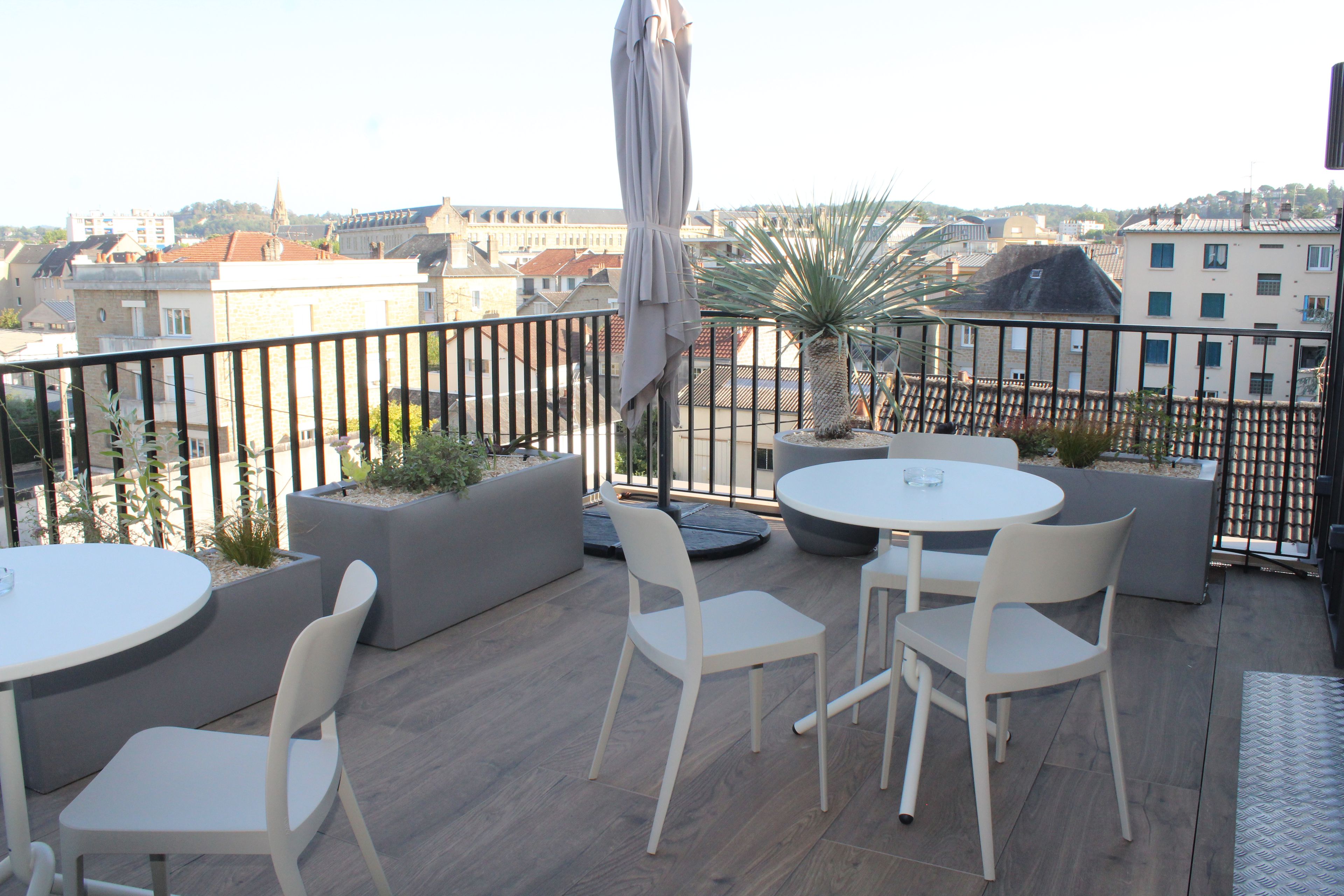 Terraço com mesa redonda e cadeiras, um vaso de planta e vista para a cidade.