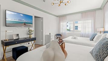 Quarto de hotel moderno com uma cama grande, uma escrivaninha com um laptop, uma televisão exibindo uma cena de praia e vista para o mar pela janela.