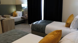 Quarto de hotel com duas camas, uma escrivaninha e uma mesinha de cabeceira.