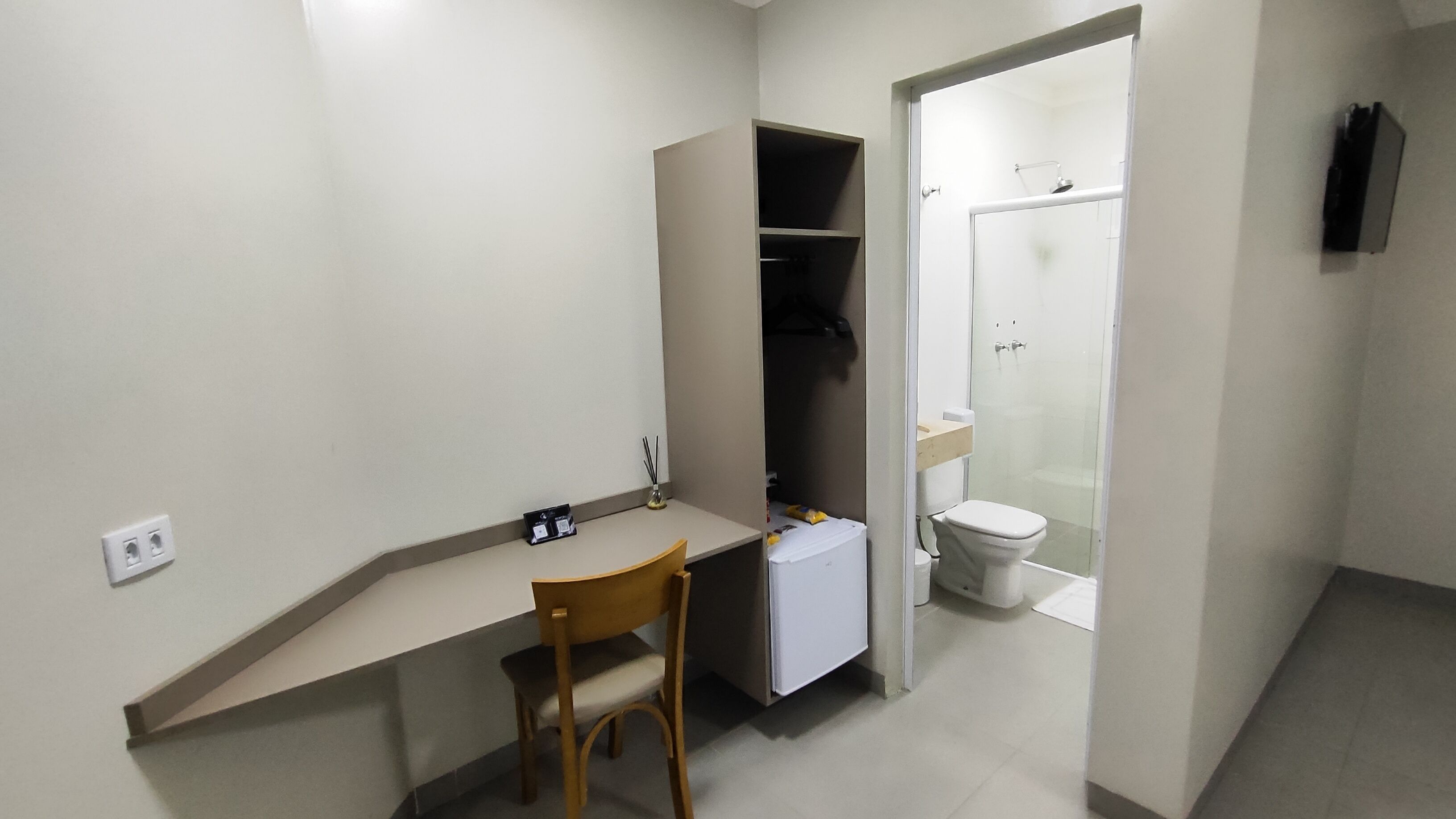 Casa de banho compacta com chuveiro, sanita e uma pequena secretária com cadeira.