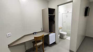 Casa de banho compacta com chuveiro, sanita e uma pequena secretária com cadeira.