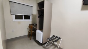 Quarto pequeno com escrivaninha, cadeira, guarda-roupa e janela.