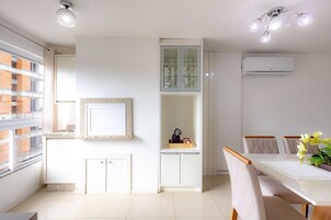 Uma cozinha moderna com geladeira embutida, sala de jantar com mesa e cadeiras, e uma janela com vista para um prédio de tijolos.