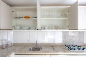 Uma cozinha com armários brancos, bancada de granito, pia de aço inoxidável e fogão a gás.