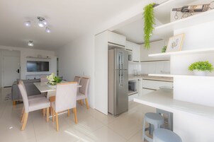 Uma cozinha moderna com frigorífico embutido, armários brancos e um espaço de refeições com mesa e cadeiras.
