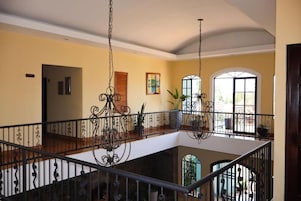Interior com vários níveis, varanda, grades de ferro forjado e lustres pendentes.