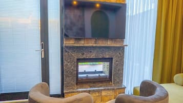 Uma sala de estar moderna com lareira de pedra, duas poltronas e vista para o exterior.