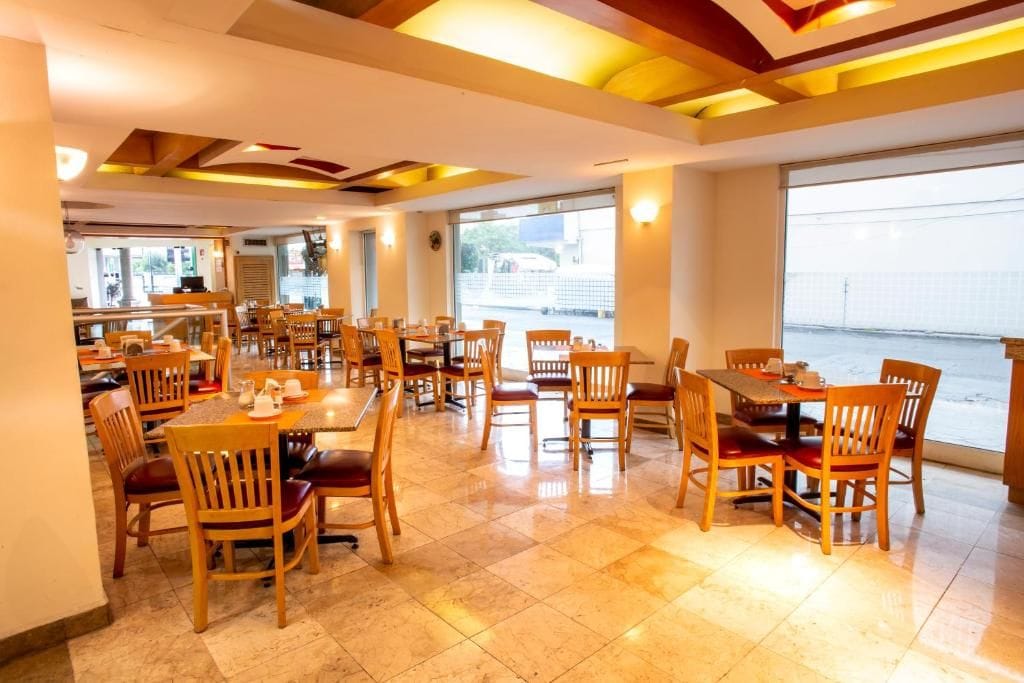 Uma sala de jantar com várias mesas e cadeiras, janelas amplas e vista para o exterior.