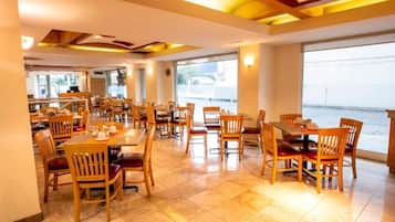 Uma sala de jantar com várias mesas e cadeiras, janelas amplas e vista para o exterior.