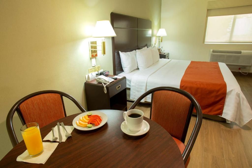 Quarto de hotel com cama, mesas de cabeceira, mesa de jantar com café da manhã e uma janela.