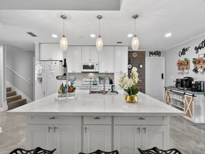Uma cozinha moderna com ilha central, armários brancos, iluminação pendente e um espaço para café.