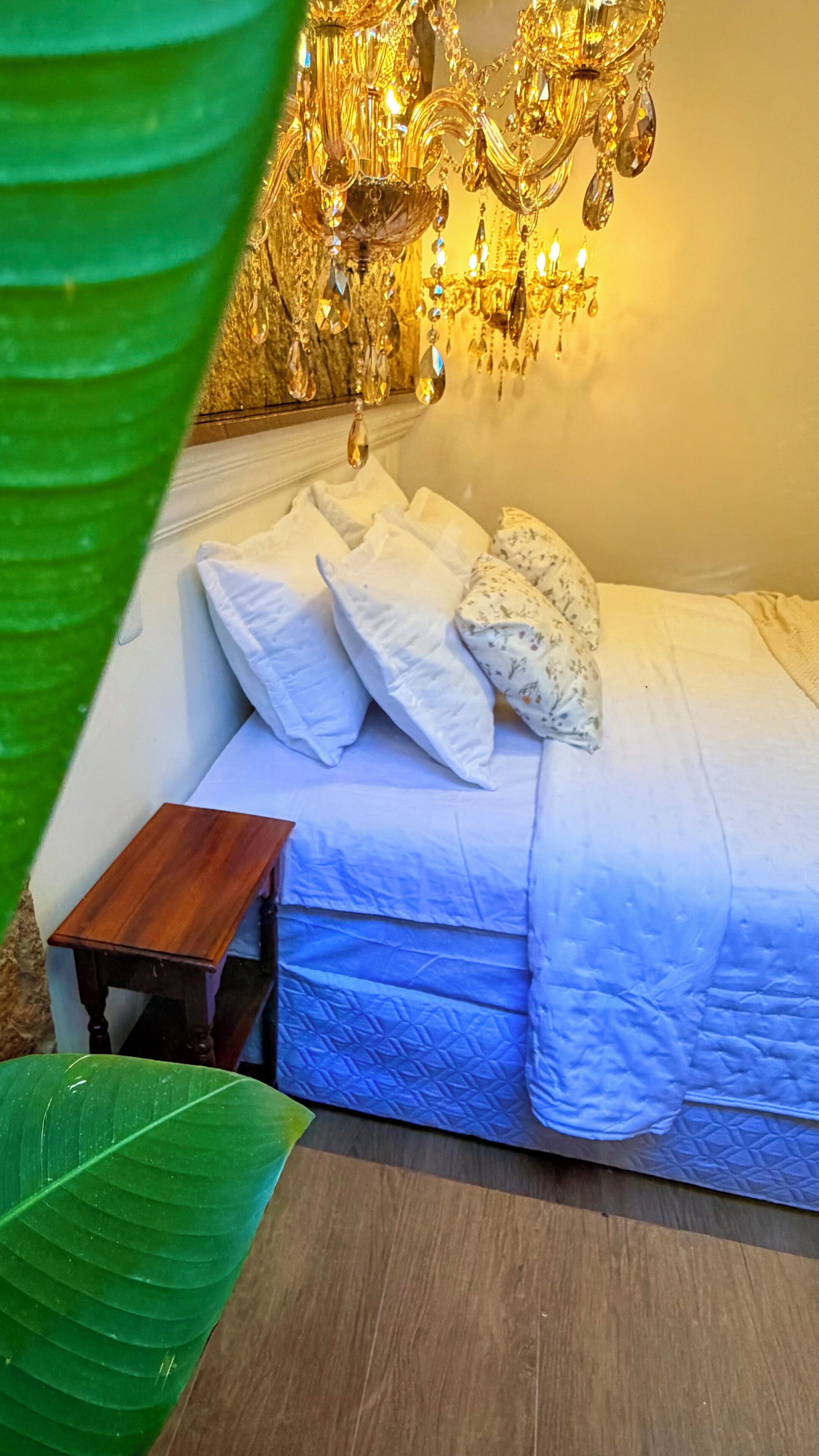Quarto com cama, almofadas, mesa de cabeceira e lustre.