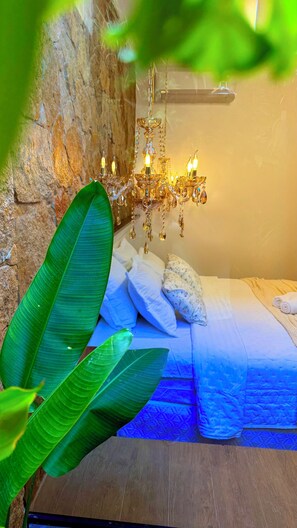 Um quarto com cama, almofadas, um candelabro e uma planta grande.