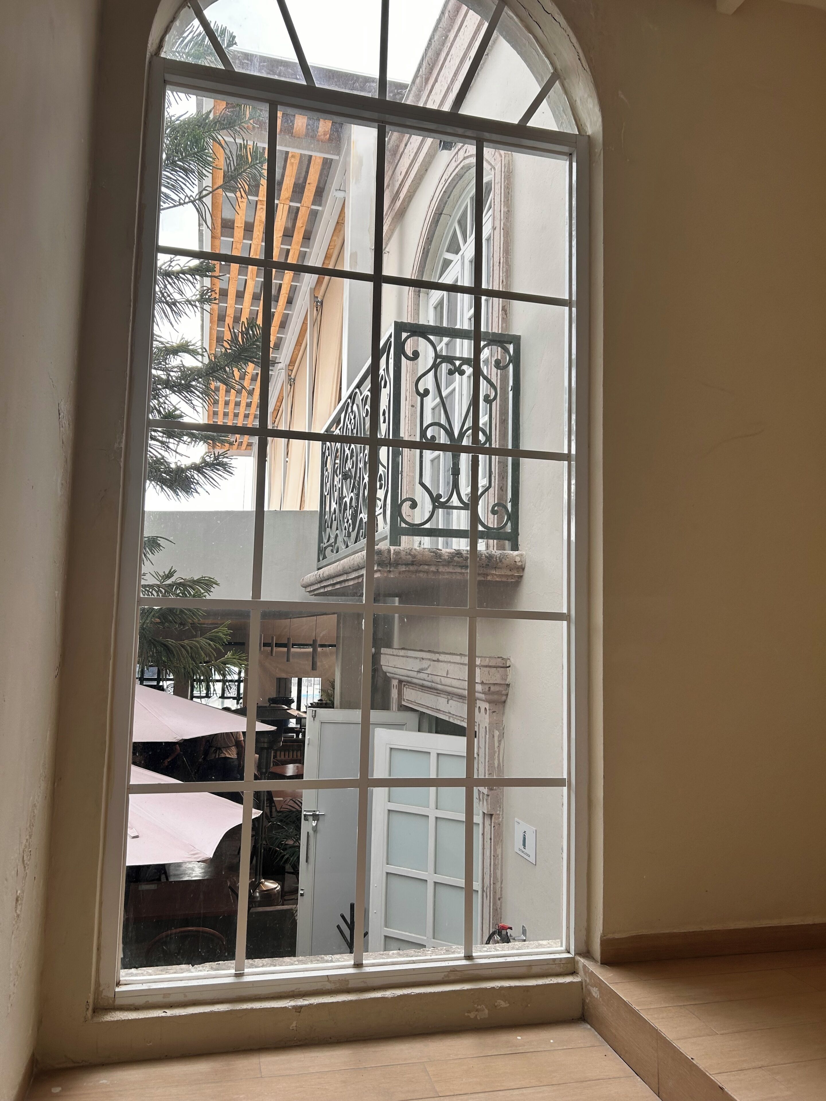 Uma janela com grade de metal decorativa, vista de um edifício com varandas e chão de azulejos.
