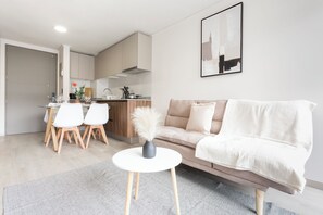 Uma sala de estar moderna com um sofá, um espaço de refeições com cadeiras e uma cozinha ao fundo.