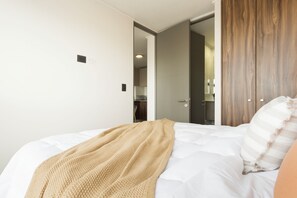 Quarto com uma cama, guarda-roupa de madeira e porta para uma casa de banho.